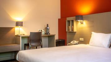 Quarto de hotel com cama, escrivaninha, cadeira e telefone.