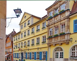 Um edifício amarelo com várias janelas, algumas com persianas azuis e caixas de flores nas varandas.