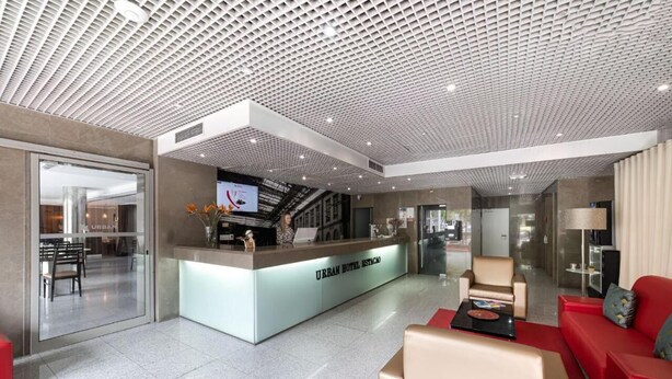 Um saguão de hotel moderno com balcão de recepção, área de estar e escada que dá acesso aos andares superiores.