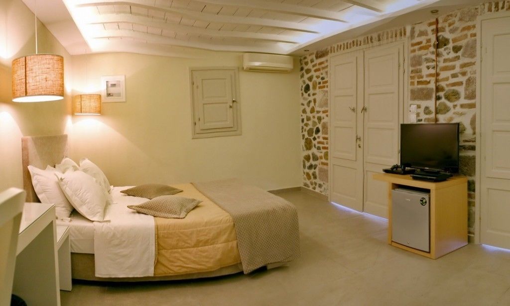 Quarto com cama, televisão sobre suporte, guarda-roupa e pequeno armário.
