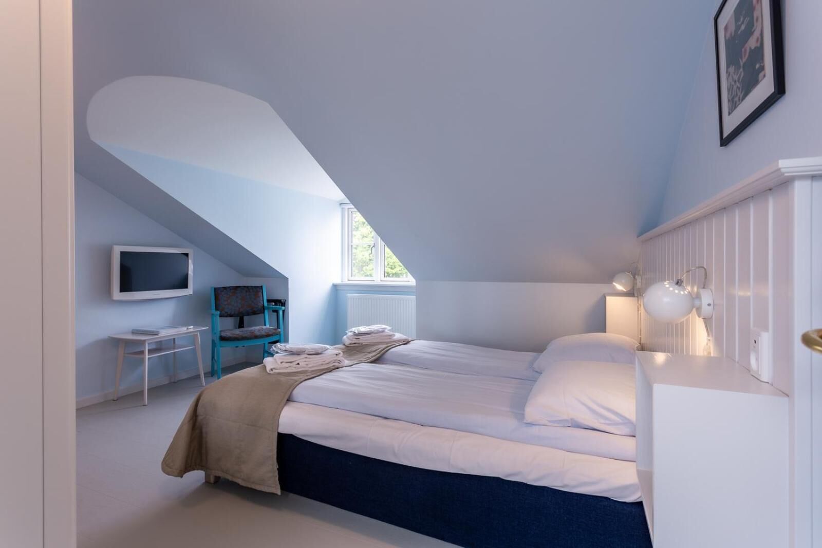 Quarto com cama, televisão, cadeira e escrivaninha.