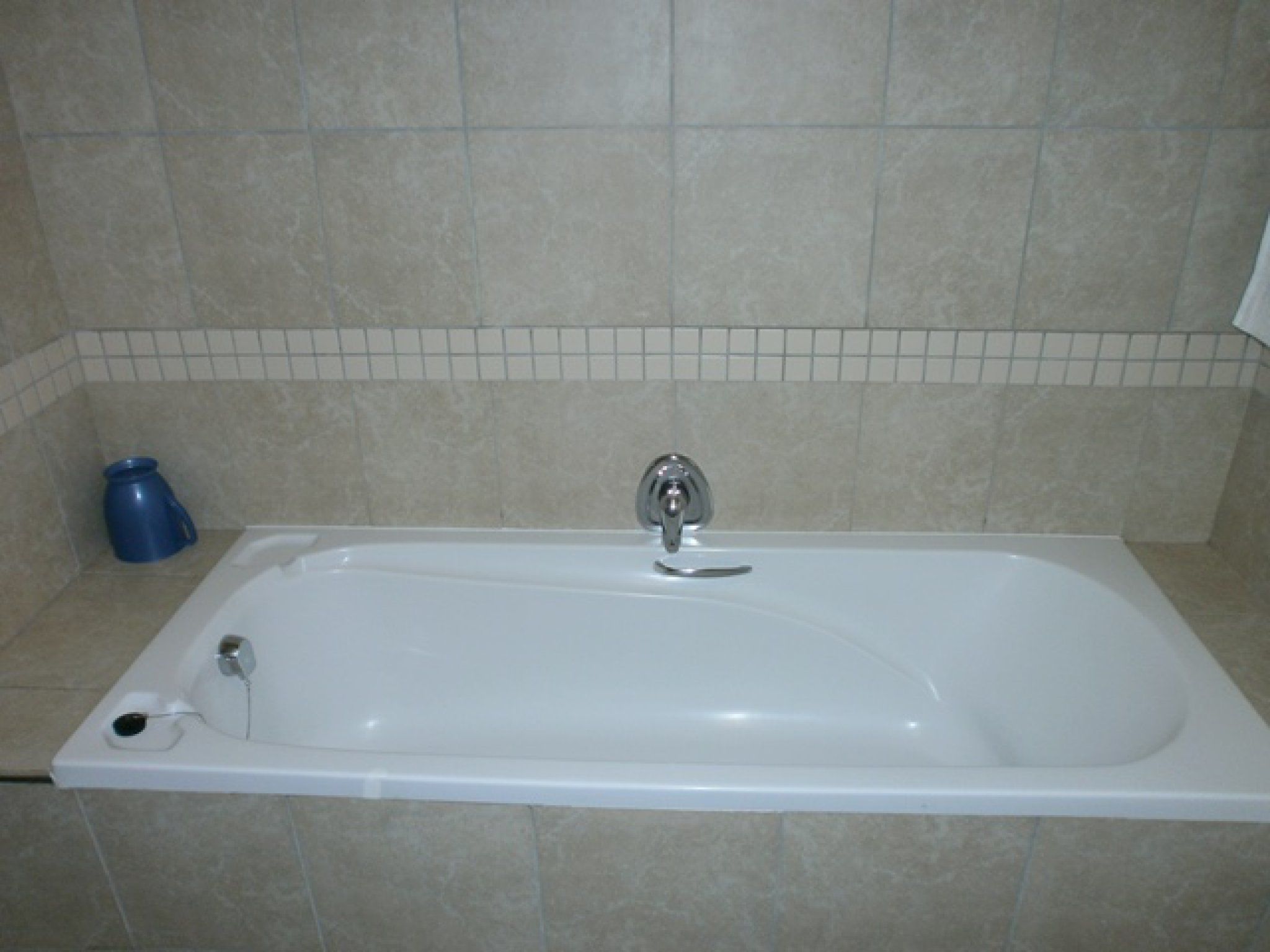 Uma casa de banho com uma banheira branca, um recipiente azul e paredes revestidas a azulejos bege.