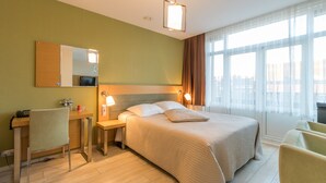 Quarto de hotel com cama, escrivaninha, cadeira, espelho e janela com cortinas.