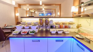 Uma área de buffet com diversos recipientes de comida e uma televisão ao fundo.