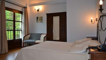 Um quarto com cama, uma cadeira, mesa de cabeceira com telefone, janela com cortinas e um quadro na parede.