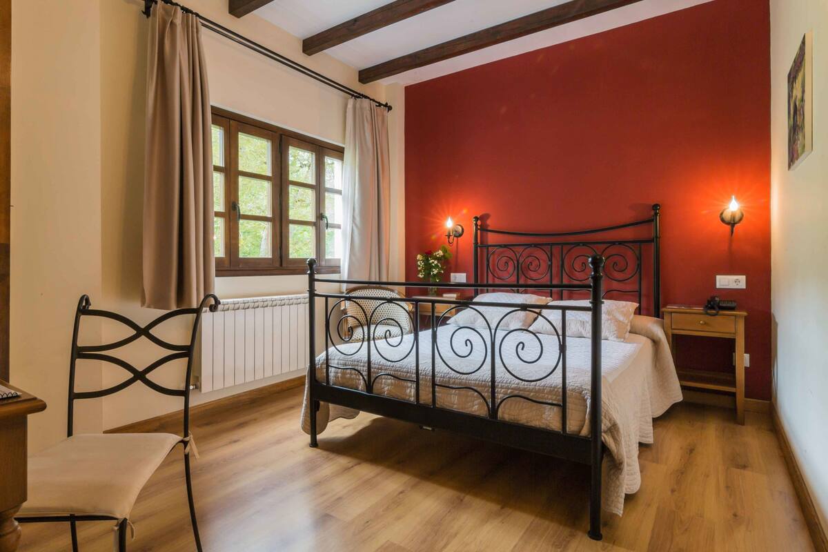 Quarto com cama, poltrona, mesa de cabeceira e janela com cortinas.