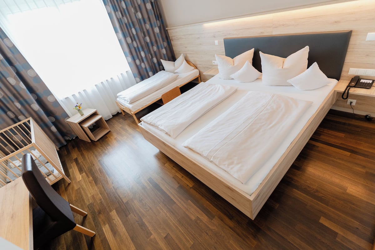 Quarto de hotel com uma cama grande, duas camas menores, uma escrivaninha e uma cadeira.