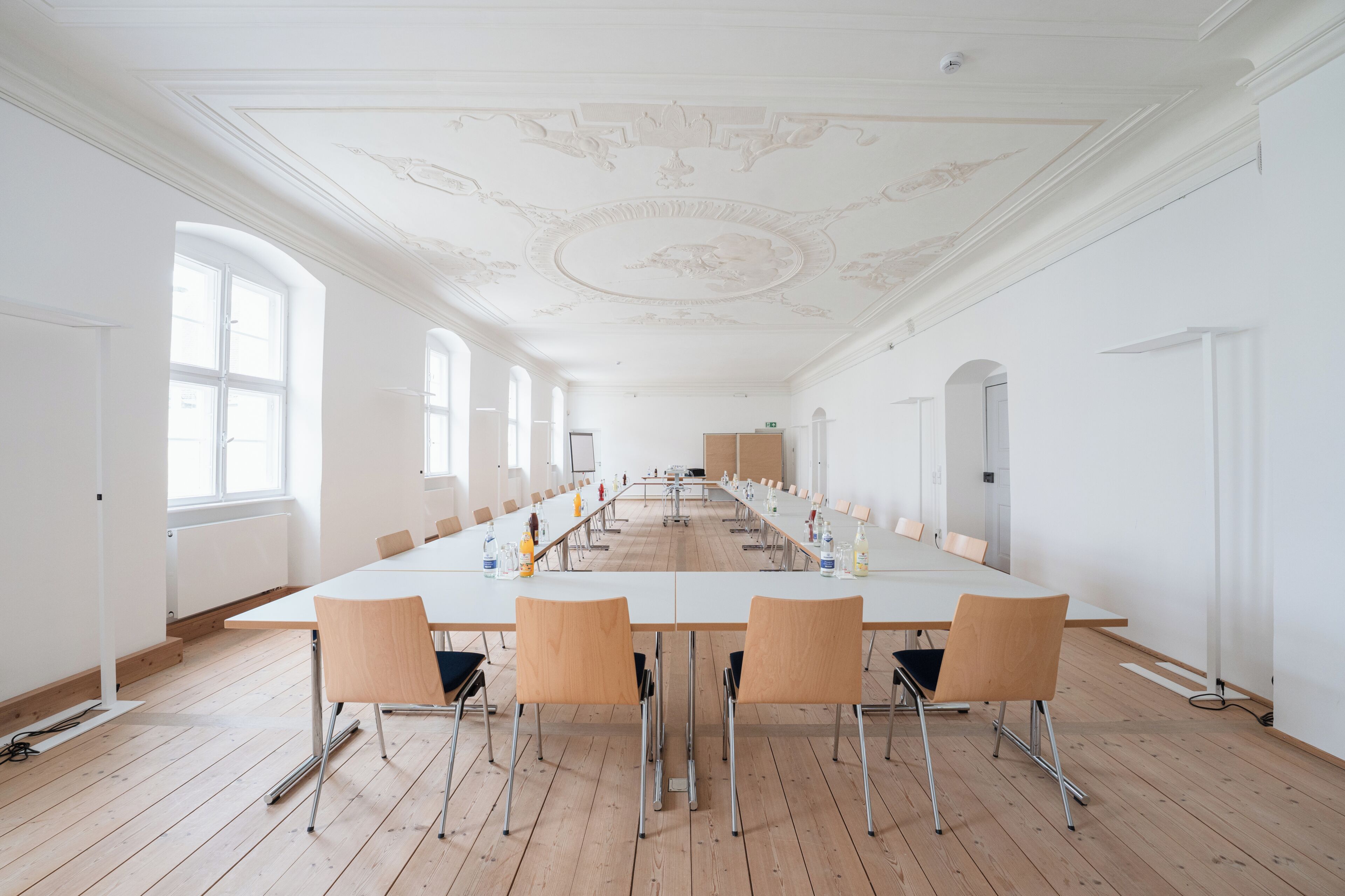Uma sala de conferências com uma longa mesa, cadeiras e teto branco com detalhes artísticos.