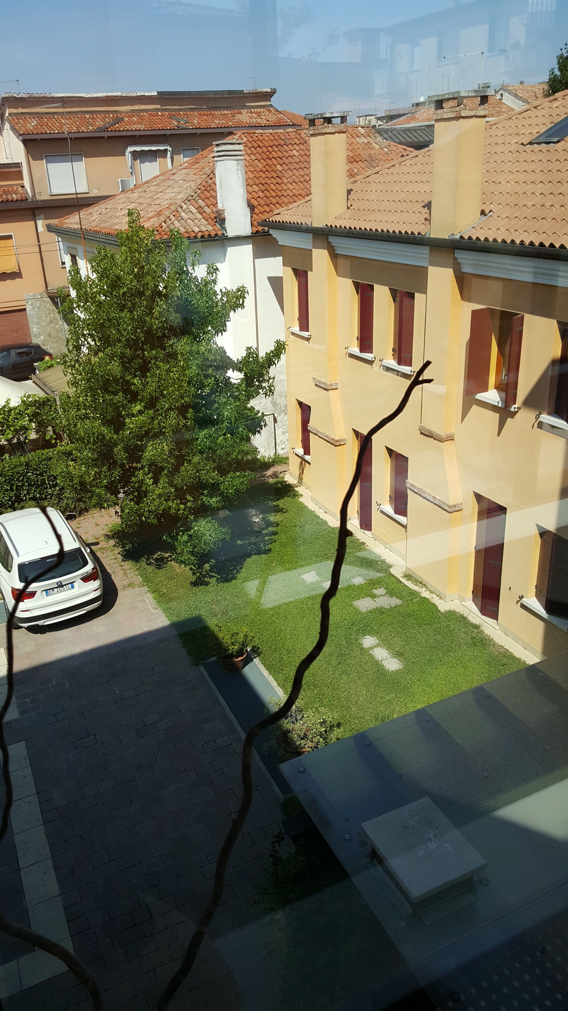 Um edifício residencial com telhado de cerâmica, uma árvore no quintal e um carro estacionado.