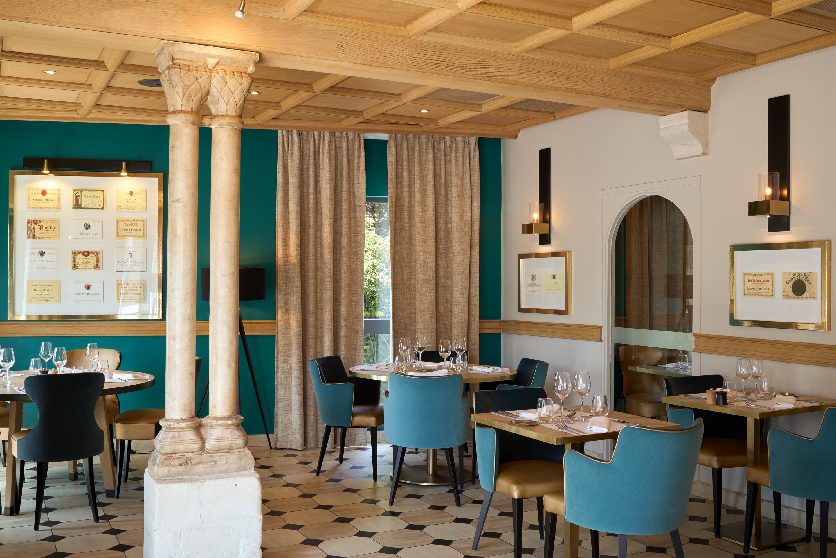 Restaurante com paredes verde-azuis, teto de madeira e chão xadrez. Mesas montadas com copos de vinho e pratos.