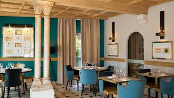Restaurante com paredes verde-azuis, teto de madeira e chão xadrez. Mesas montadas com copos de vinho e pratos.