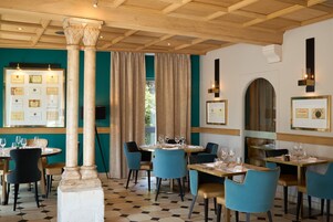 Restaurante com paredes verde-azuis, teto de madeira e chão xadrez. Mesas montadas com copos de vinho e pratos.