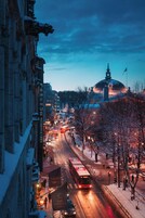 Rua urbana ao entardecer com um edifício imponente em formato de cúpula ao fundo.