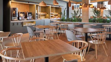 Um café moderno com mesas e cadeiras de madeira, balcão de café e plantas dentro.