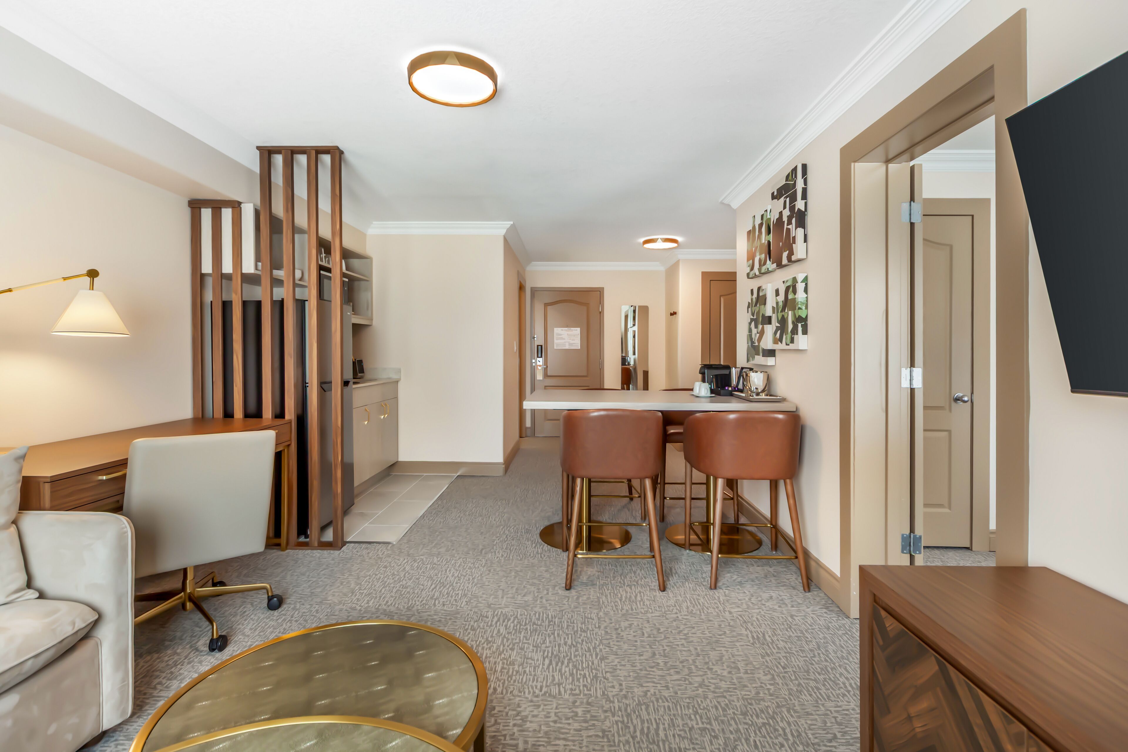 Quarto de hotel moderno com área de refeições, sofá, escrivaninha e televisão na parede.