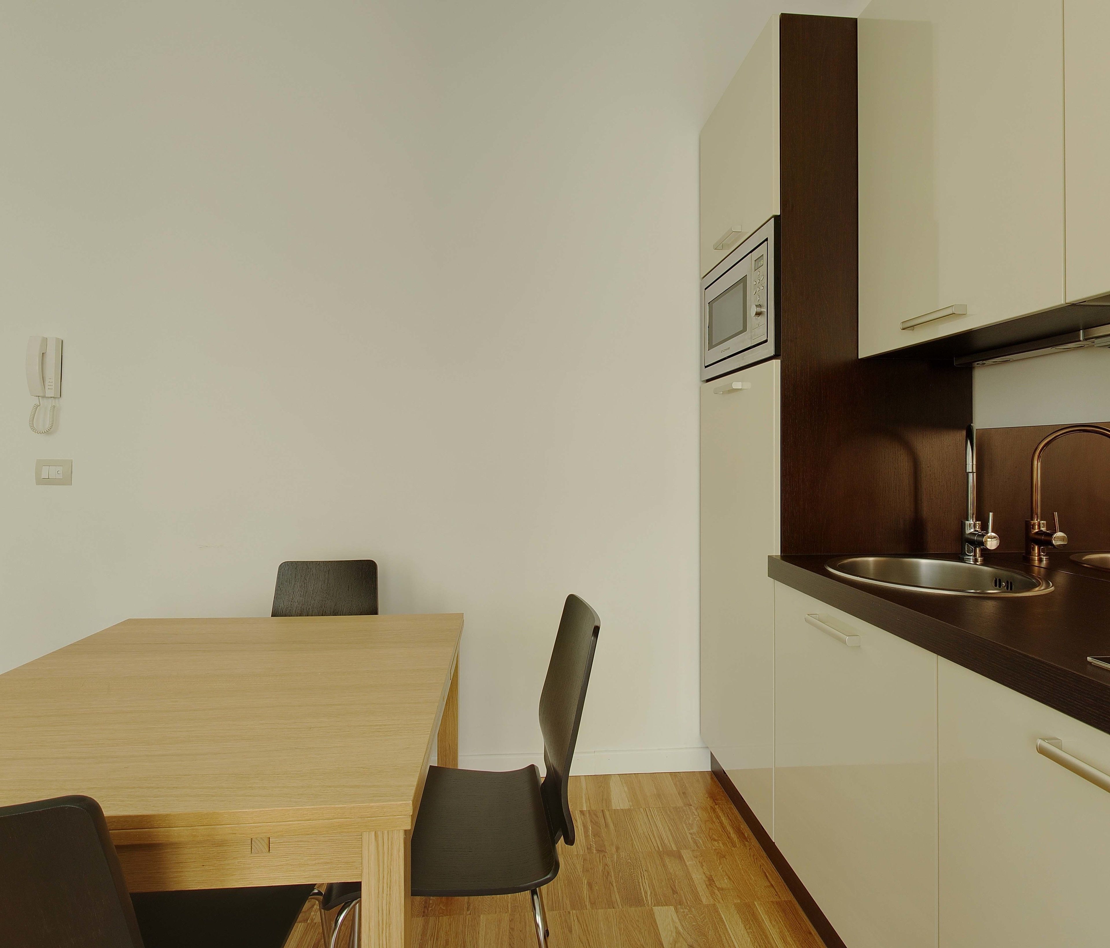 Uma cozinha moderna com uma mesa de jantar de madeira, duas cadeiras, micro-ondas embutido e uma pia de aço inoxidável.
