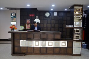 Bancada de recepção com um relógio, um quadro emoldurado e uma placa indicando a área de recepção.