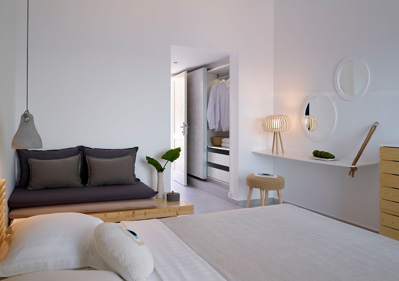 Quarto moderno com cama, sofá, mesa de cabeceira, luminária, espelho e guarda-roupa.