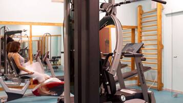 Academia com equipamentos de ginástica, esteira e uma pessoa utilizando uma máquina.