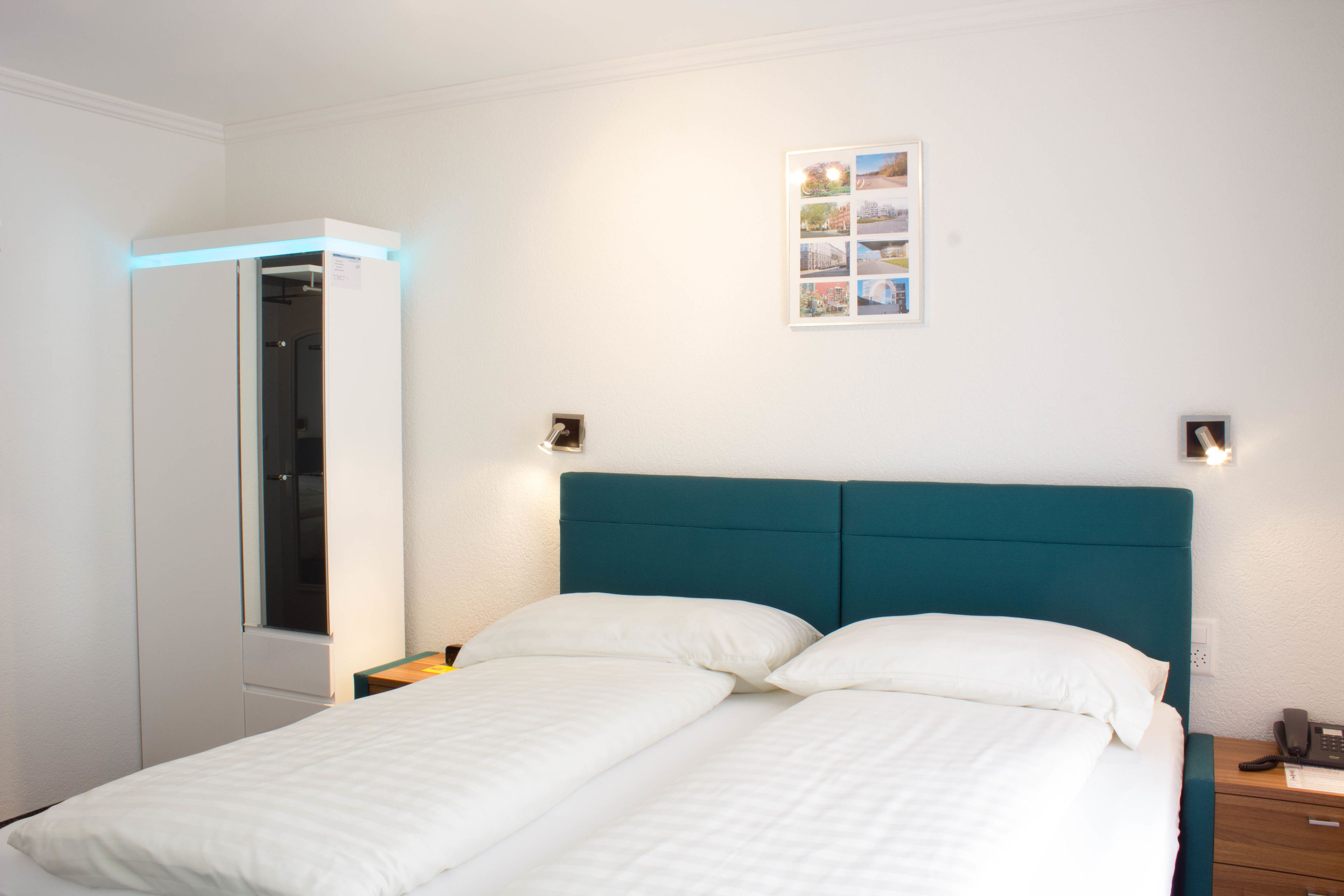 Quarto de hotel com cama, mesas de cabeceira, guarda-roupa e luminária.