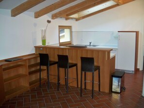 Uma cozinha compacta com bancada de madeira, três banquetas, geladeira e janela sobre a pia.