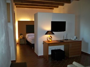 Quarto de hotel com uma cama, uma mesa com luminária, uma televisão e um pequeno armário.