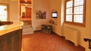 Um corredor amplo com teto de madeira, piso ladrilhado, uma grande janela com várias divisórias e um pequeno espaço de estar com mesa e cadeiras.