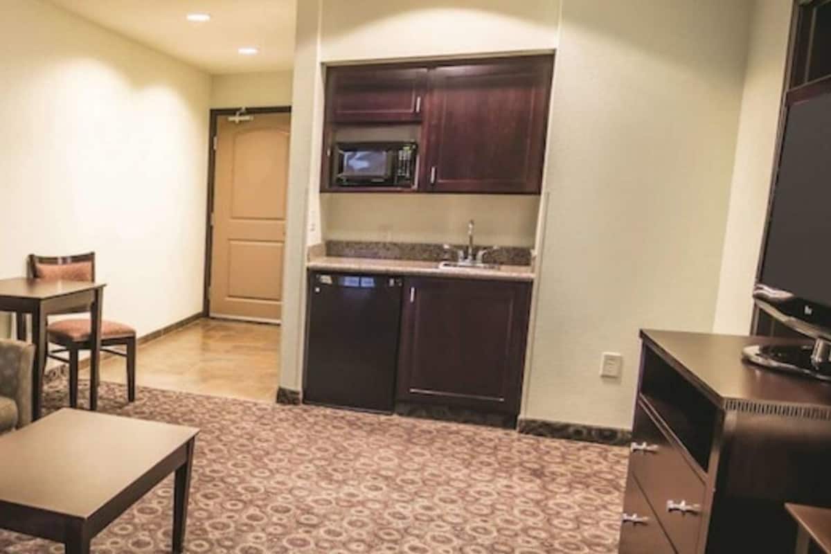 Sala de estar com sofá, mesa pequena, abajur e televisão. Há uma cozinha com micro-ondas, pia e armários.