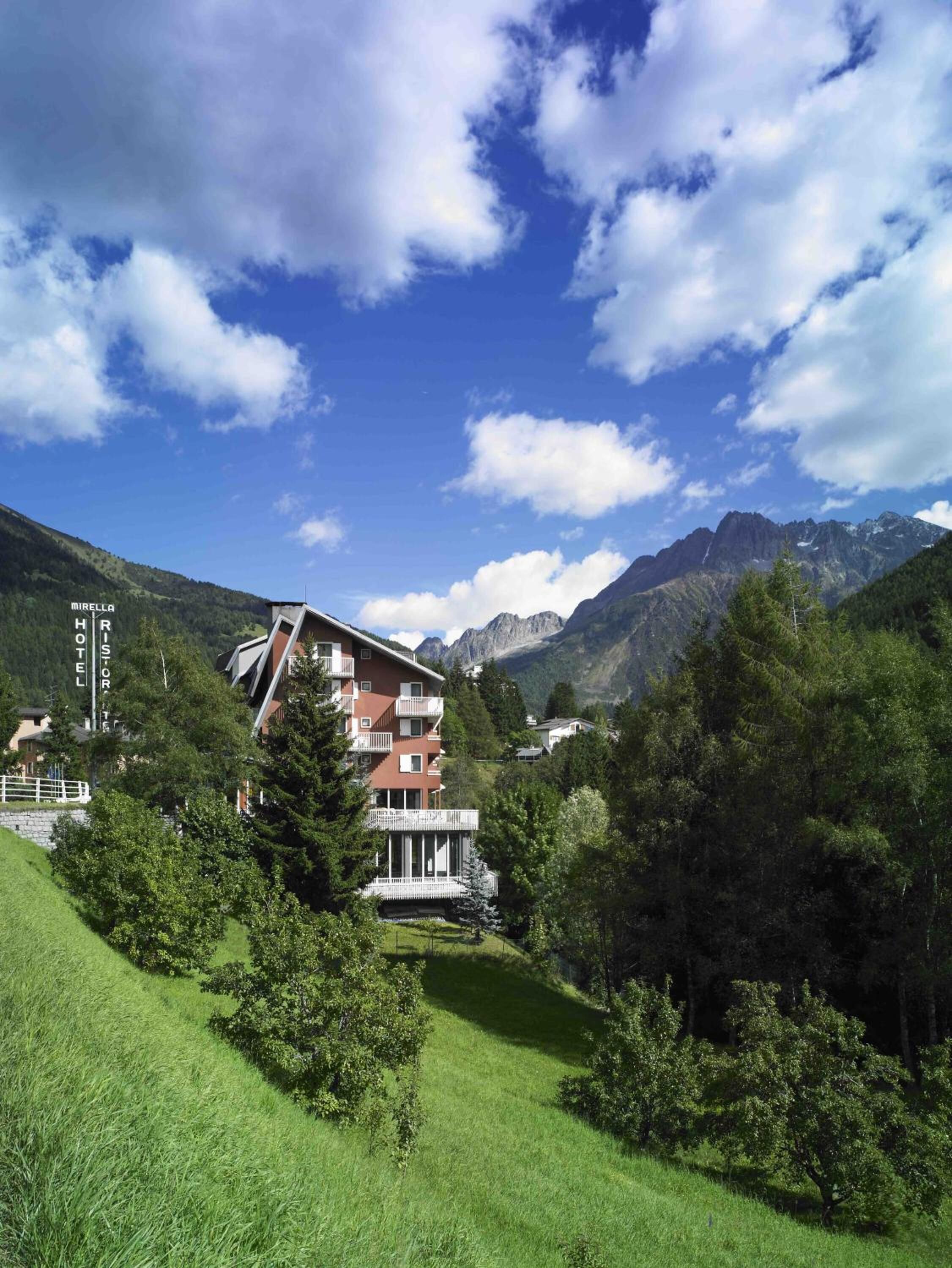 Um hotel com fachada vermelha, várias varandas e vista para montanhas e vegetação.