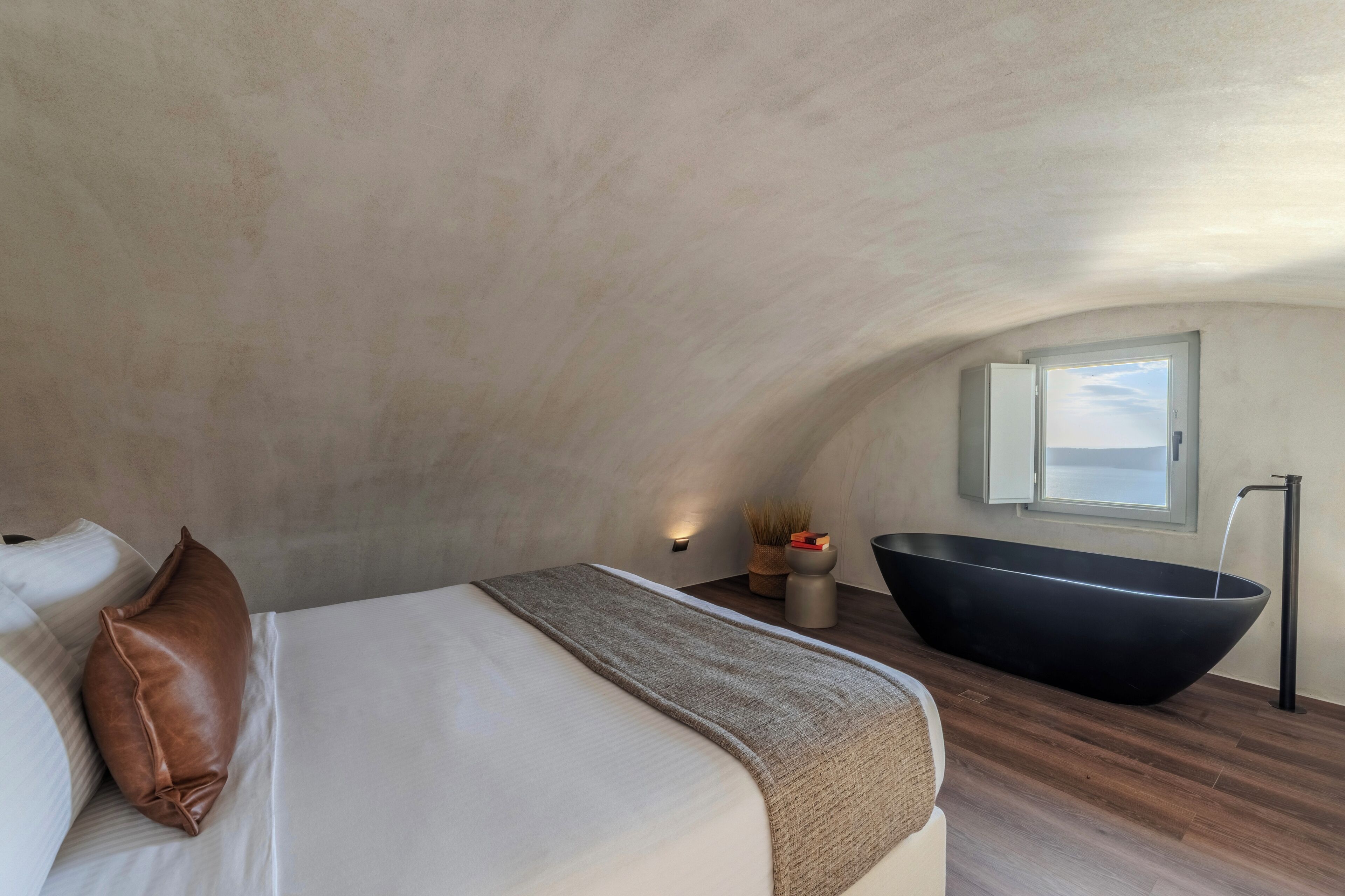 Quarto com uma cama, travesseiro marrom, banheira preta e uma janela.