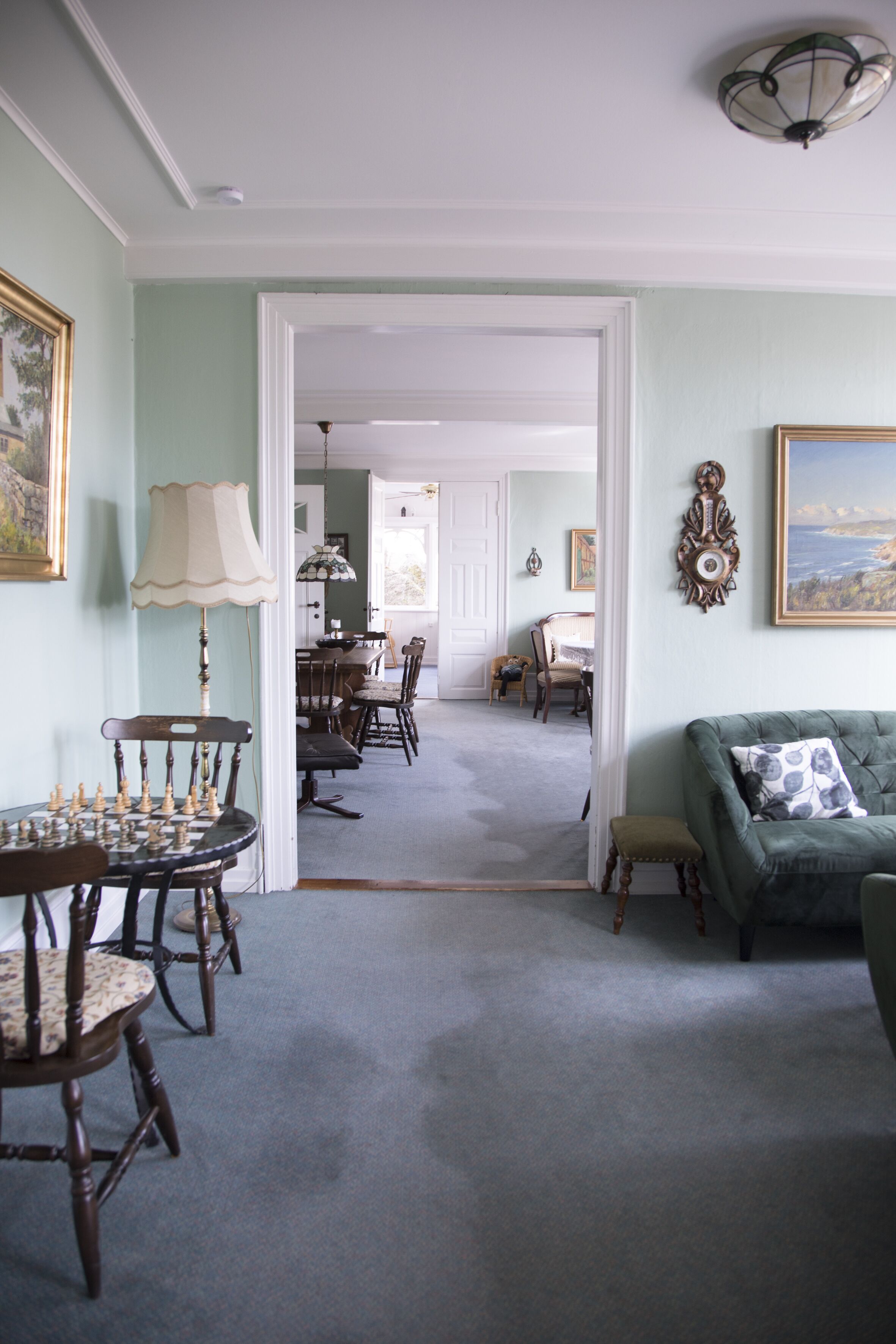 Um quarto com uma mesa de jantar, cadeiras, um sofá verde e um abajur.