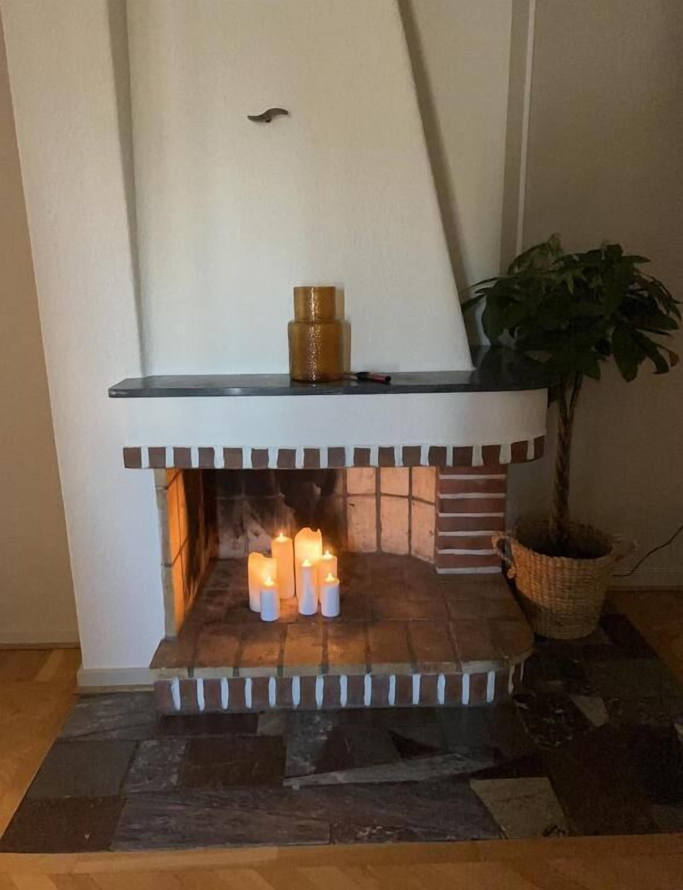Lareira com prateleira, planta em vaso e velas.
