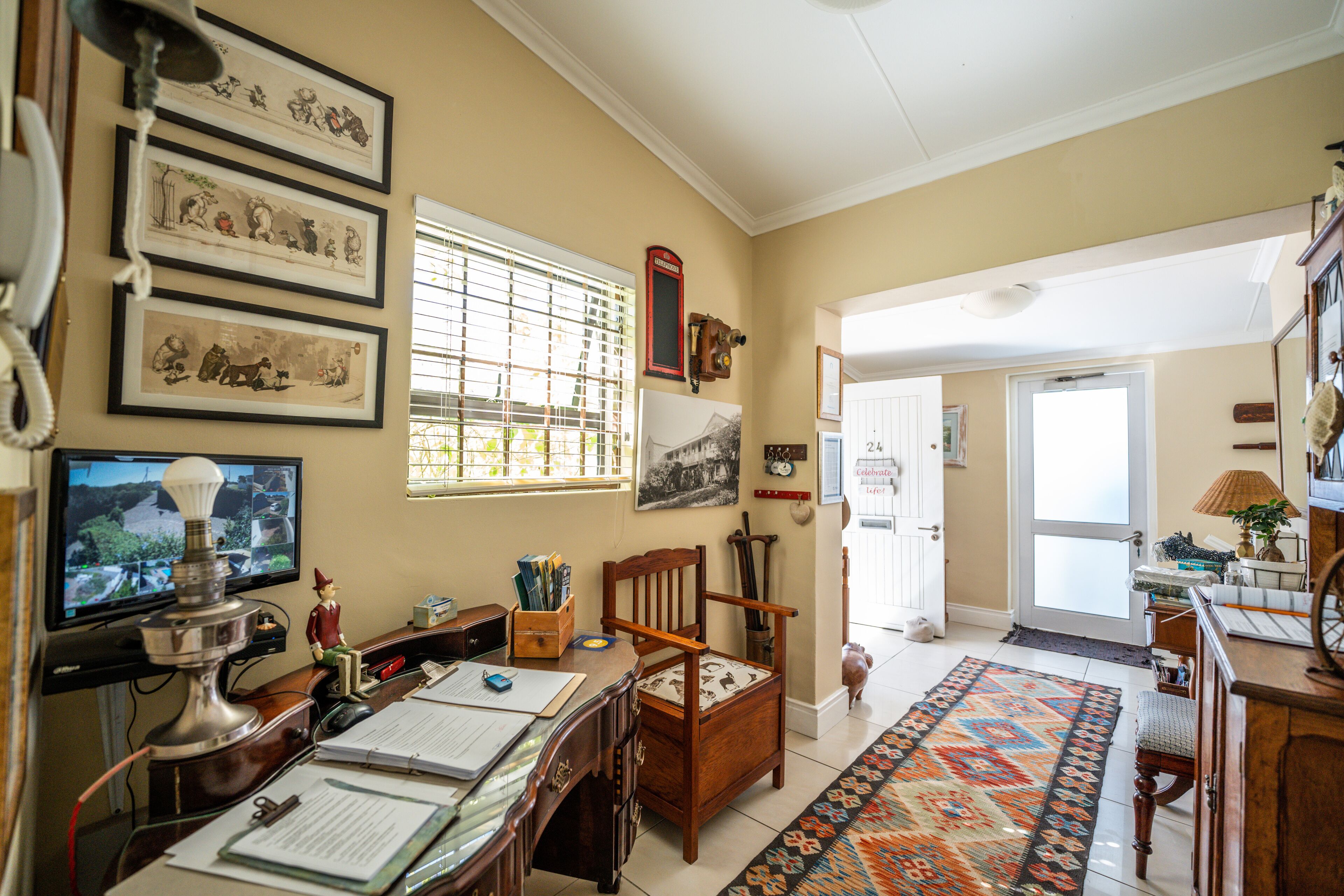Escritório em casa com mesa, cadeira, computador e vários objetos de decoração, incluindo quadros e um relógio.