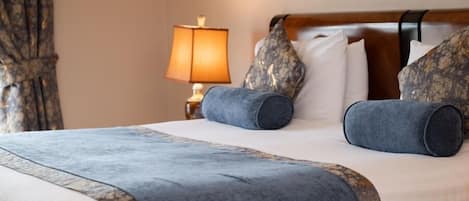 Cama bem arrumada com manta e travesseiros azuis, luminária na mesa de cabeceira e um quadro na parede.