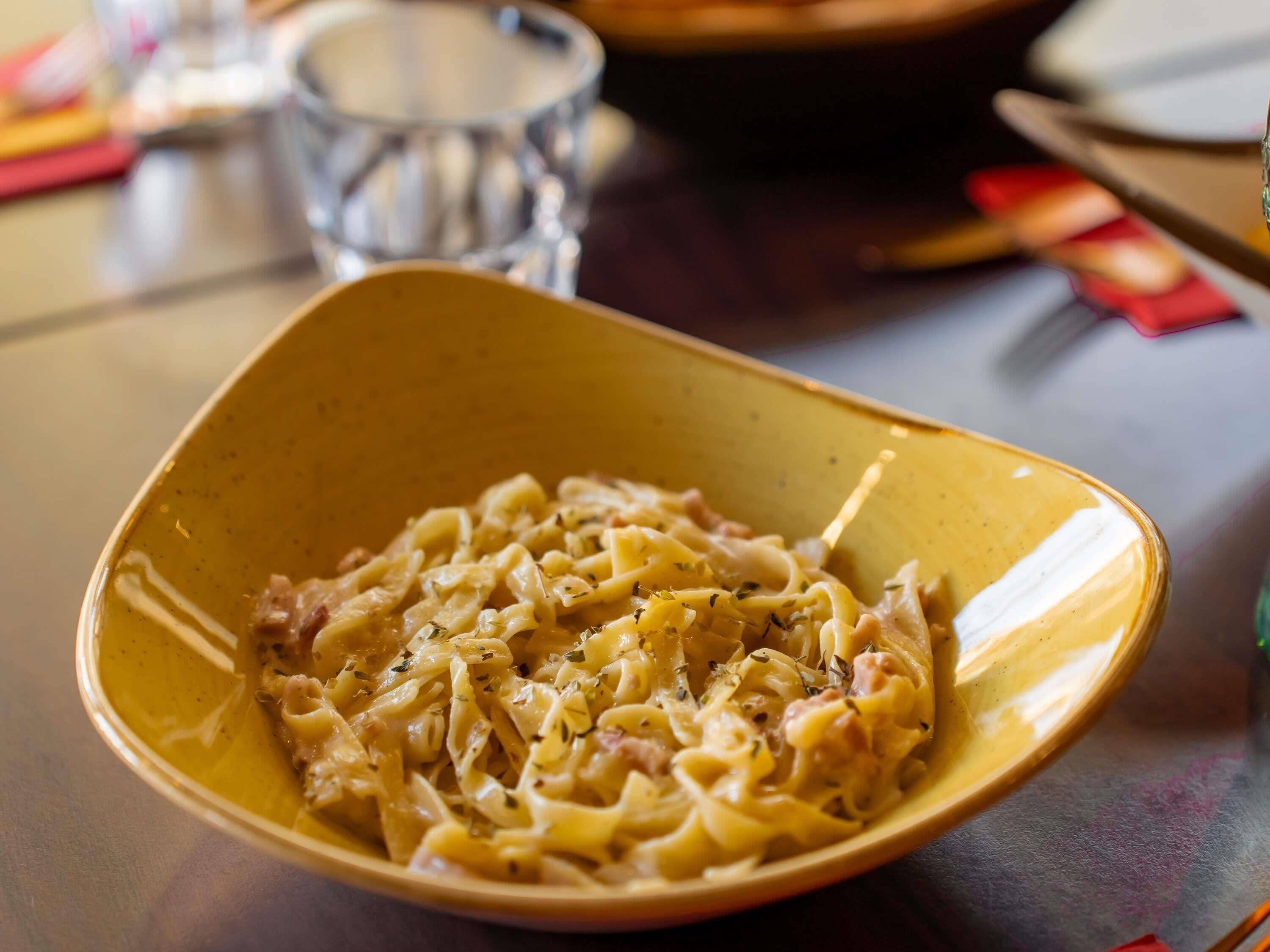 Uma tigela de massa com molho cremoso, possivelmente fettuccine, sobre uma mesa.