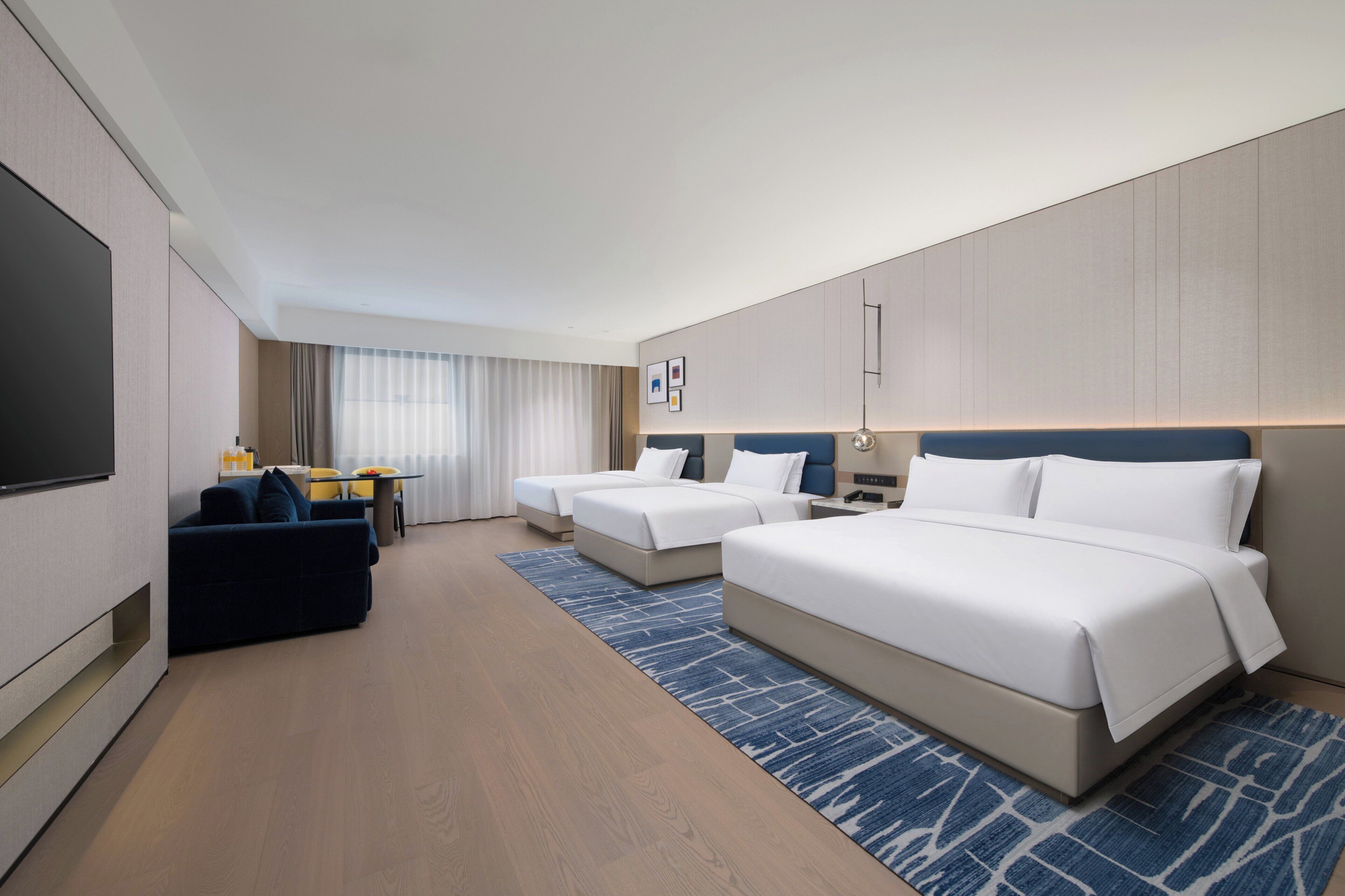 Quarto de hotel moderno com cama grande, sofá, escrivaninha e televisão.