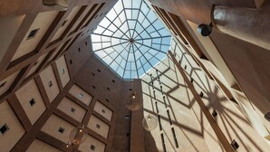 Um átrio amplo com pé direito alto, claraboia, design geométrico no teto e luminárias esféricas pendentes.