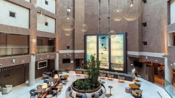 Um lobby espaçoso com área de estar central, várias mesas de jantar e luminárias esféricas penduradas.