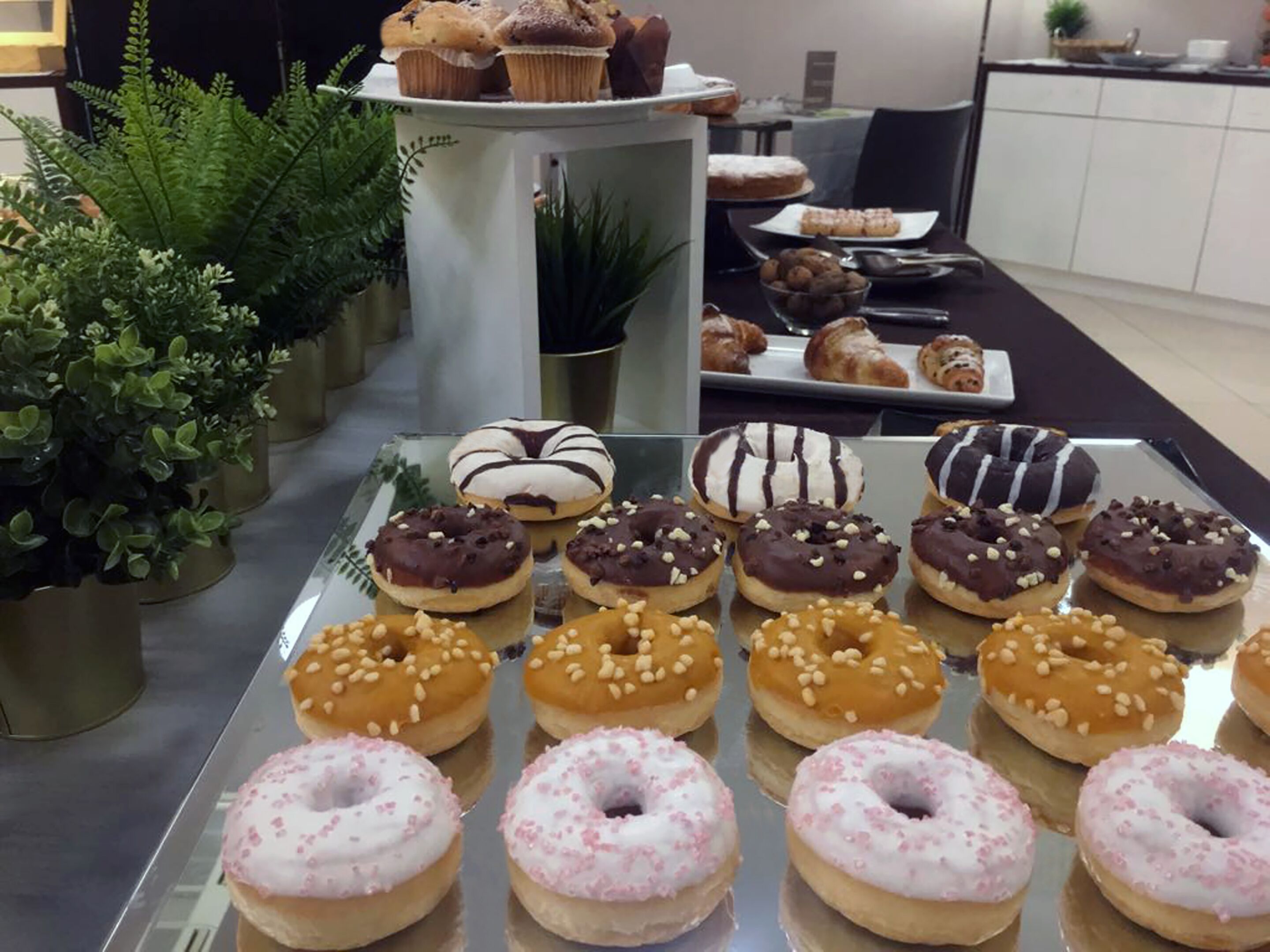 Exposição de diversos doces e donuts em bandejas, com vários tipos de coberturas e decorações.