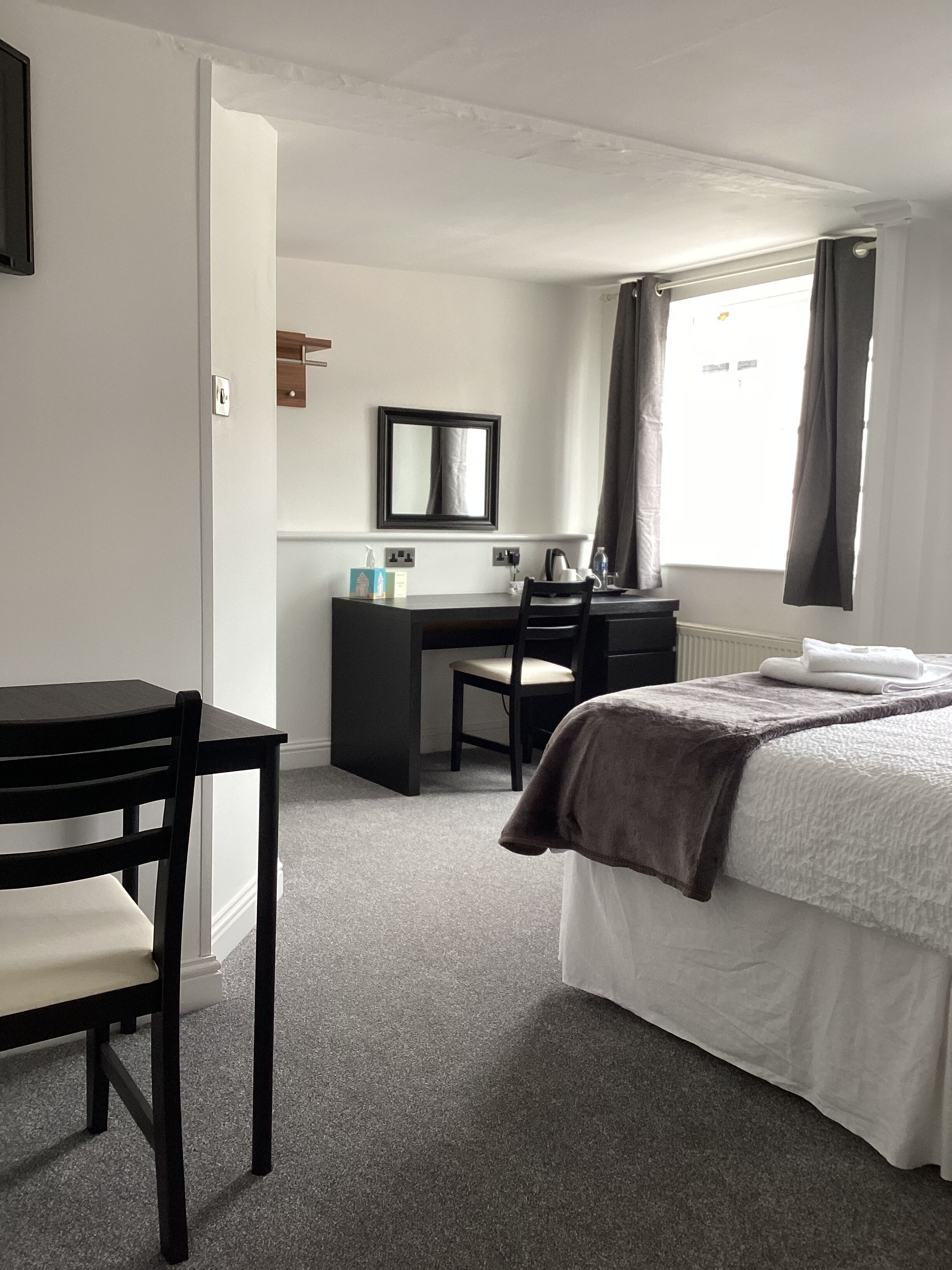 Quarto de hotel com cama, escrivaninha, cadeira, espelho e janela com cortinas.