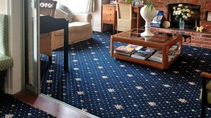 Uma sala de estar com carpete azul estampado, mesa de centro de madeira com livros, lareira, espelho grande e um lustre.