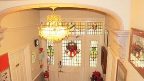 Um hall imponente com um candelabro, uma porta decorada com uma guirlanda e um extintor de incêndio.