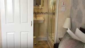 Quarto de hotel com uma cama, mesa de cabeceira com abajur, banheiro com chuveiro e porta que dá para outro quarto.