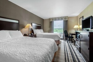 Quarto de hotel com duas camas, uma escrivaninha com televisão, uma cadeira e um armário.