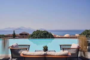 Uma área à beira da piscina com espreguiçadeiras e vista para o mar.