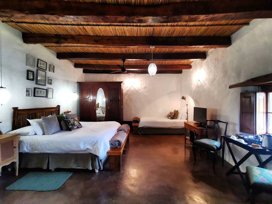 Quarto rústico com teto de madeira, duas camas, uma escrivaninha com cadeira e uma televisão.