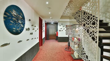 Um corredor de hotel com tapete vermelho, arte de parede com tema de peixes, escada com design de treliça branca e um armário com artigos de higiene pessoal.