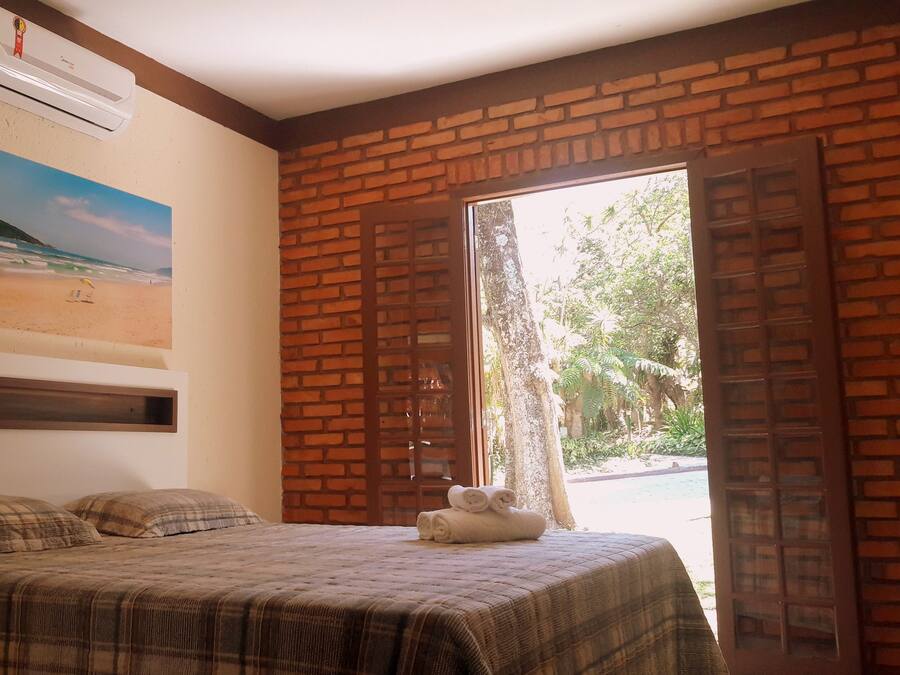 Um quarto com uma cama, um quadro de uma praia e uma parede de tijolos.