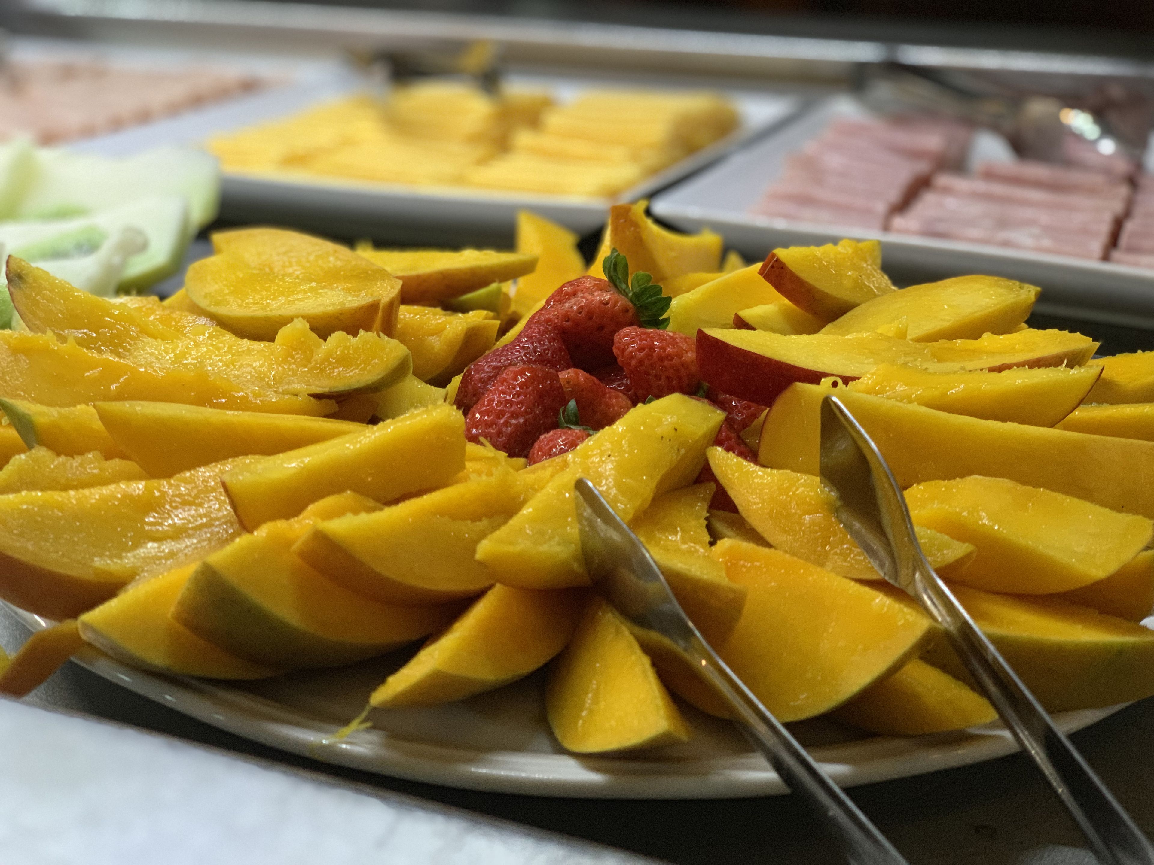 Buffet com diversas opções de frutas, incluindo mangas e morangos.