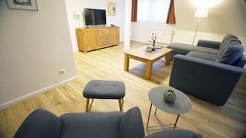 Sala de estar com sofá, mesa de centro e televisão sobre um móvel de madeira.